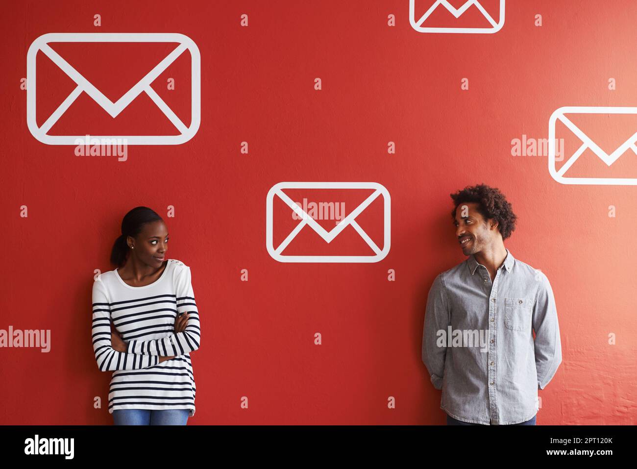 Getting the message across. A young man and woman standing against a red wall full of email ...