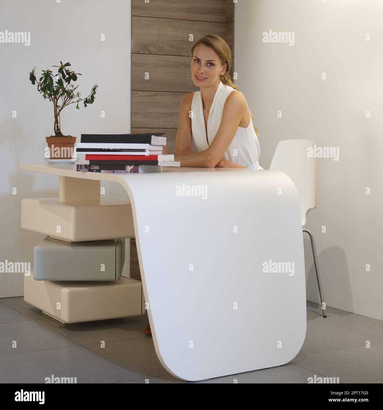 Pretty office worker sitting behind the desk in clear bright room ...