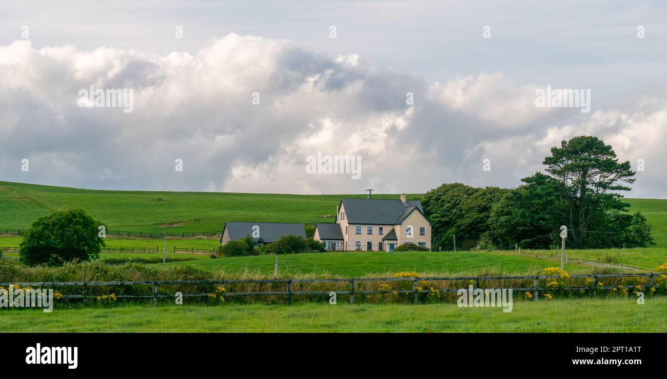 A large farmhouse among the green fields of Ireland. Cloudy sky over ...