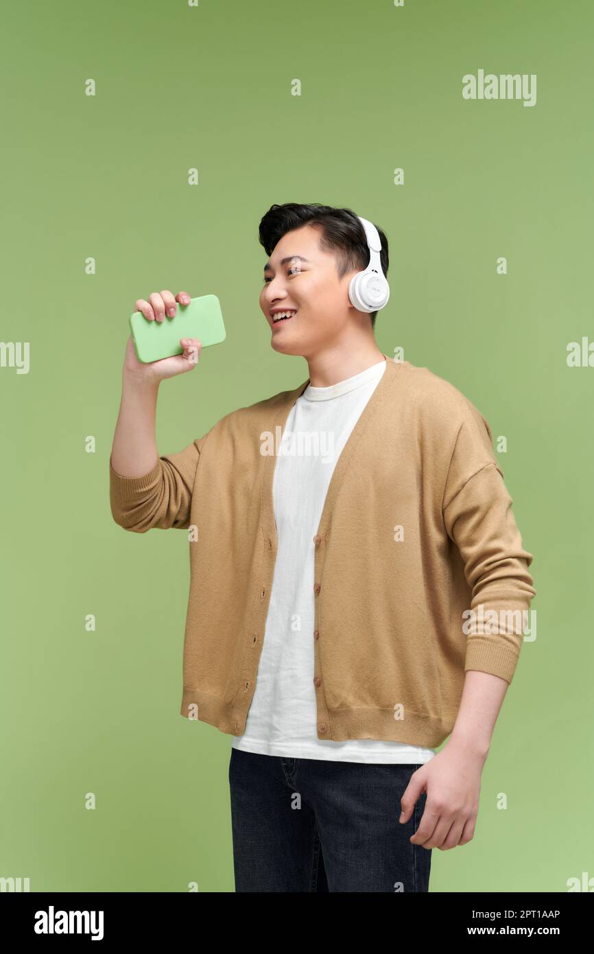 Portrait of overjoyed asian guy singing song and using smart phone as ...
