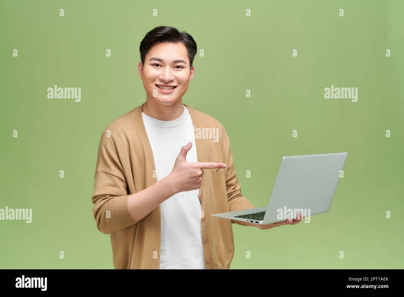 a smiling young handsome Asian man holding laptop computer while ...