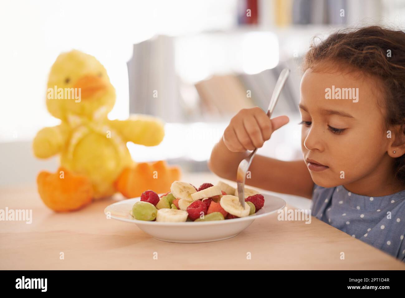 Breakfast with her best friend. a cute little girl eating fruit salad ...