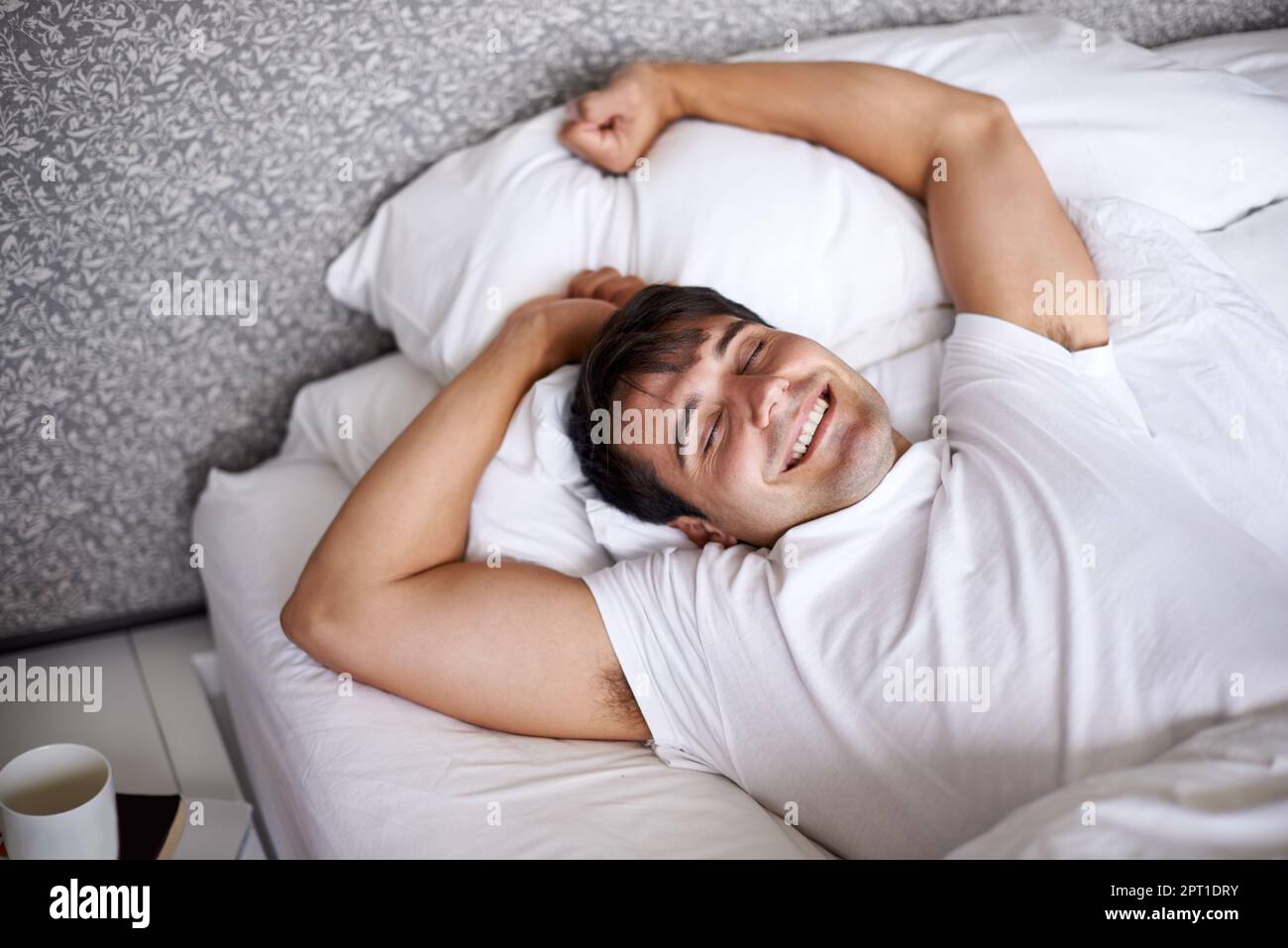 Waking up with a smile. a young man stretching in bed while waking up Stock Photo - Alamy