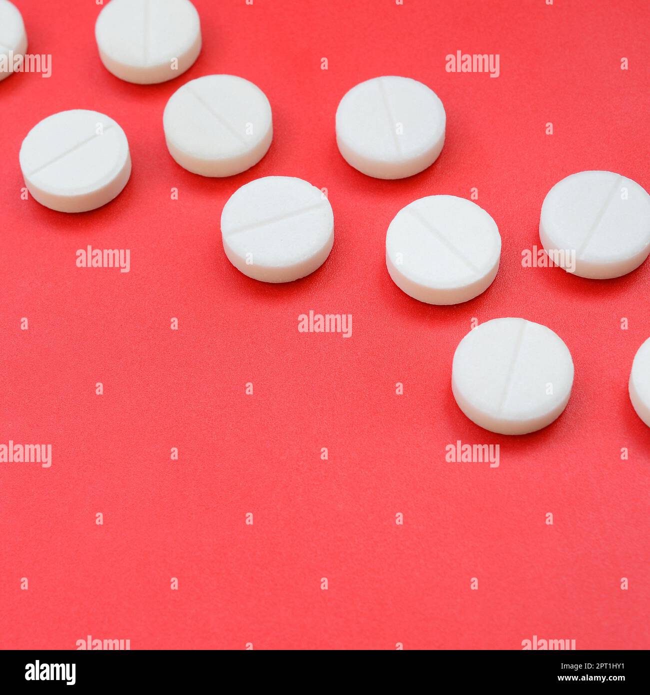 A few white tablets lie on a bright red background surface. Background ...