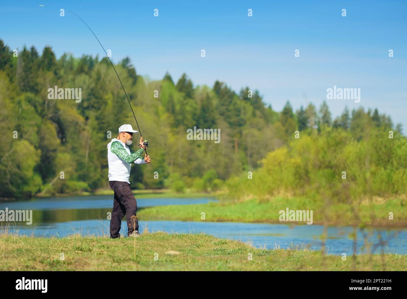 Fisherman with a spinning rod catching fish on a river at sunny summer ...
