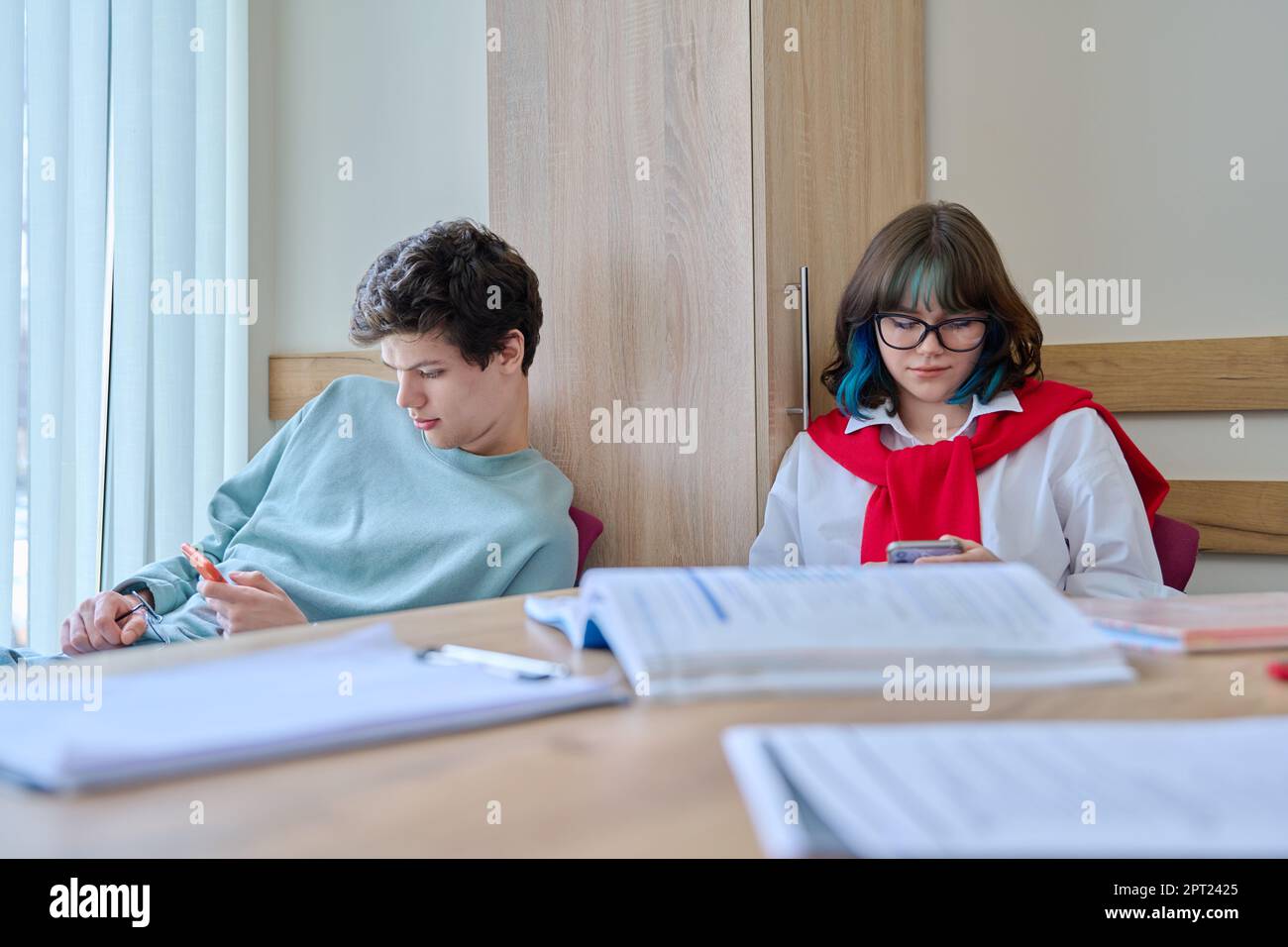 Teenage students sitting on break in classroom, resting using ...