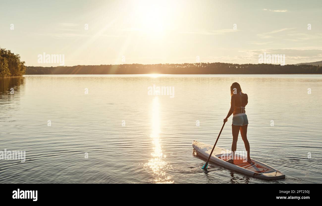 Gone paddling. an attractive young woman paddle boarding on a lake ...