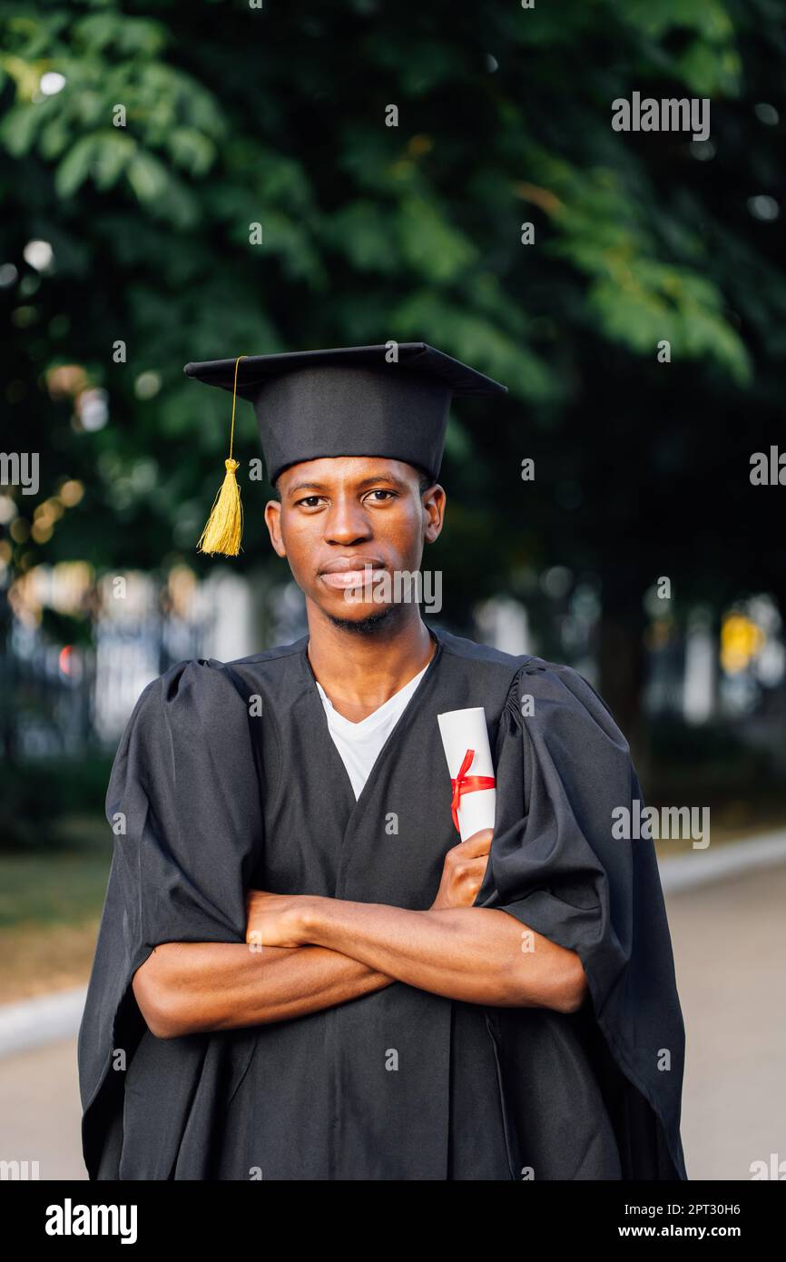 Smiling afro american graduate from university stand outdoors in black ...
