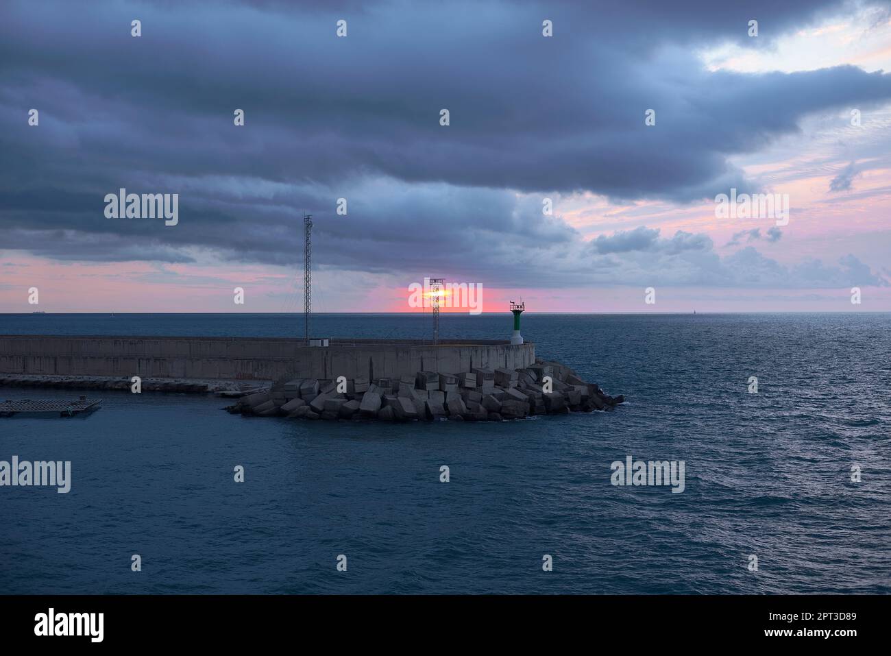 Sunrise from green lighthouse on maritime breakwater.Rocks, jetty, blue ...