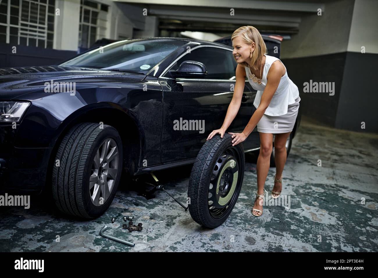 Changing a tyre is easy for her. A beautiful young woman changing her ...