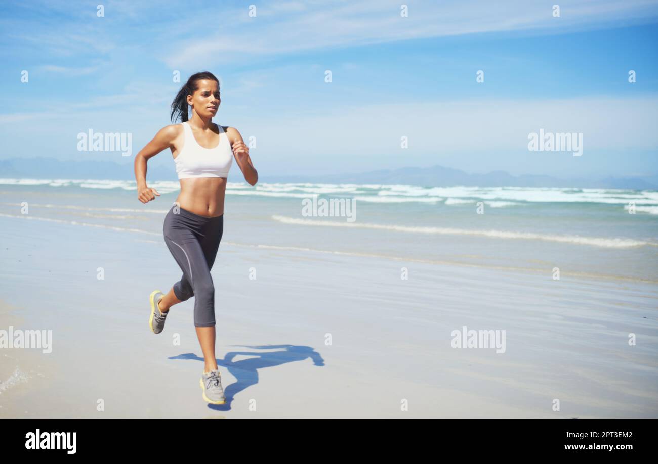 Getting her jog on. Full length shot of a young woman running along the seashore Stock Photo - Alamy