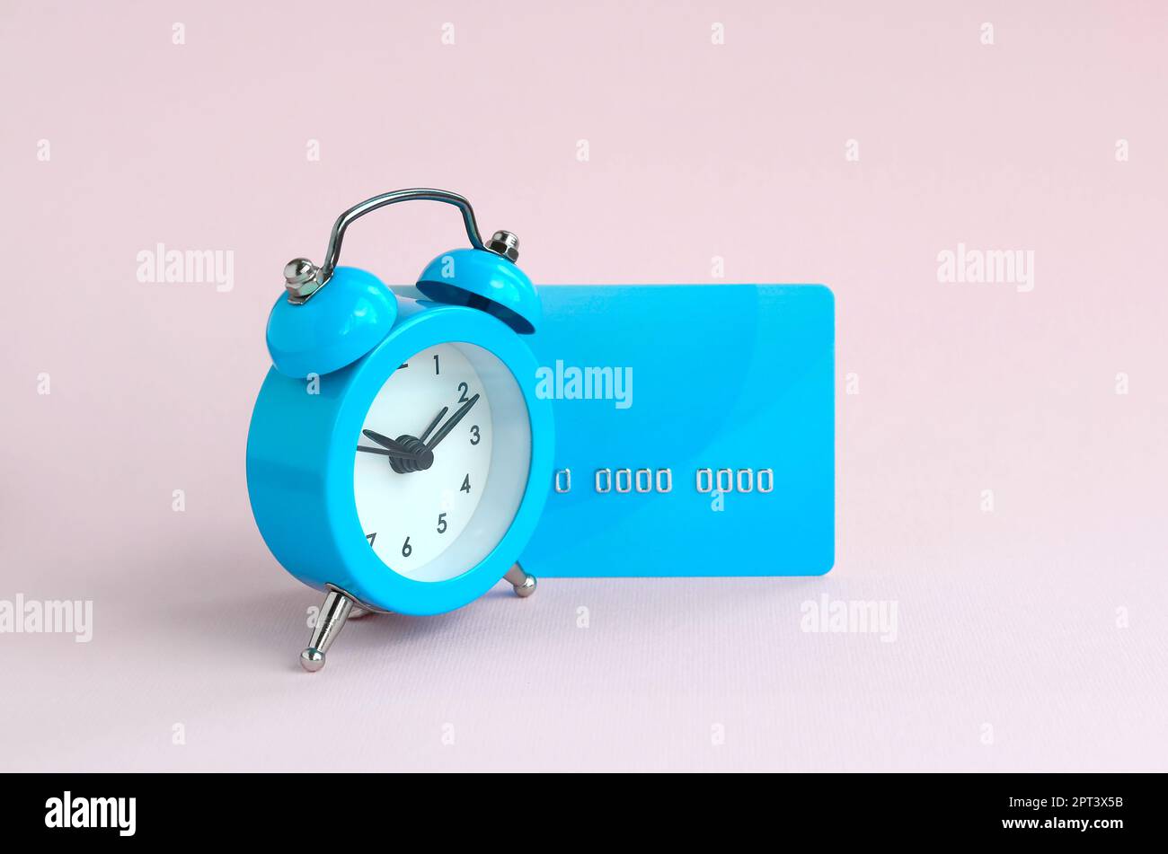 Small blue alarm clock is next to blue credit card. The concept of ...