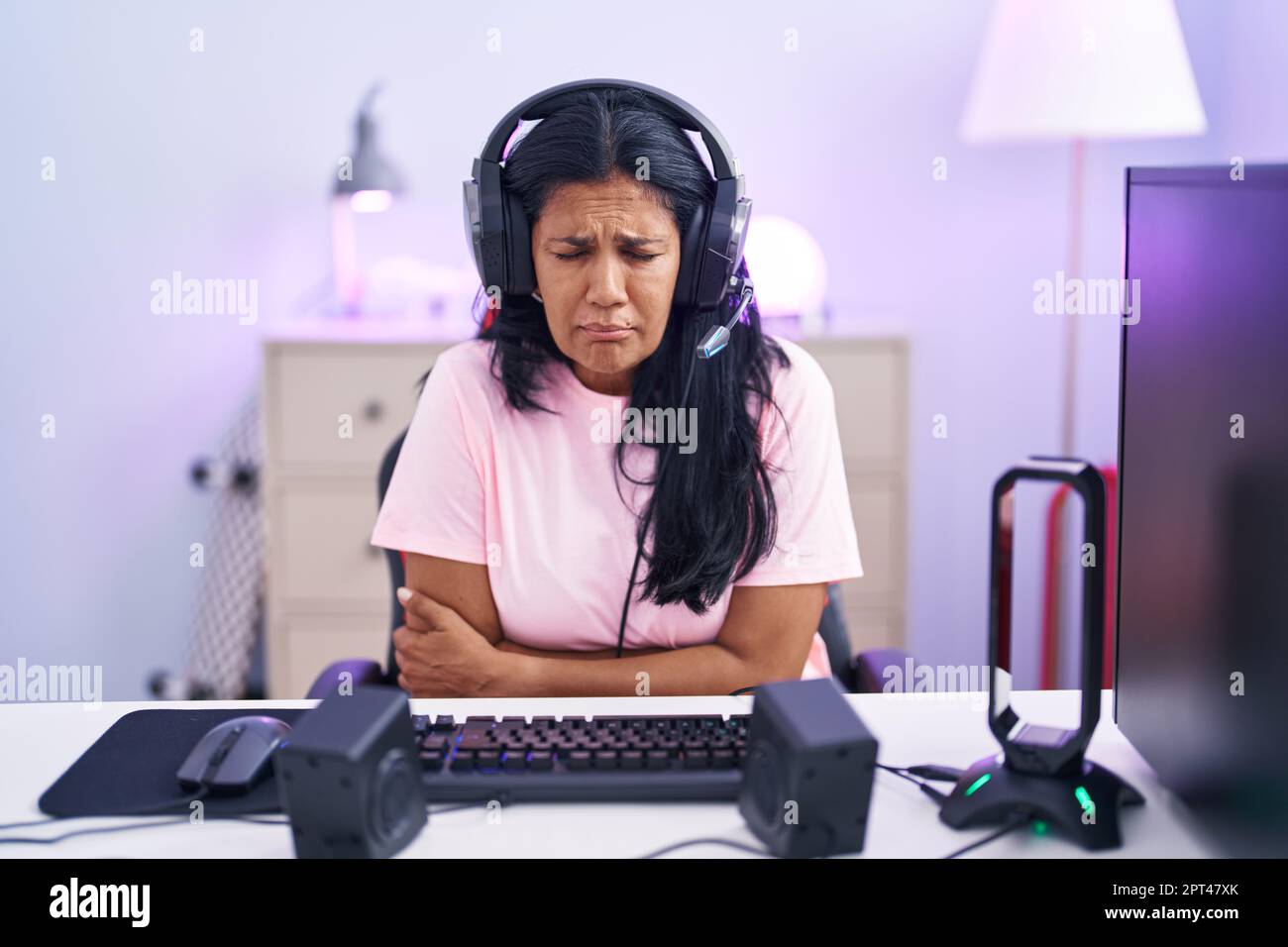 Mature hispanic woman playing video games at home with hand on stomach ...