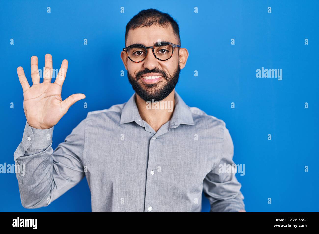 Middle east man with beard standing over blue background showing and ...