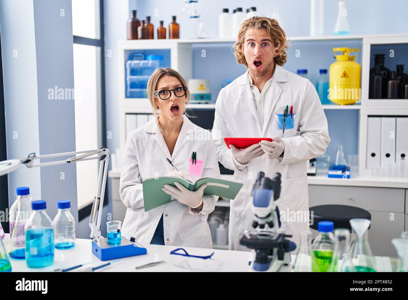 Two people working at scientist laboratory in shock face, looking ...