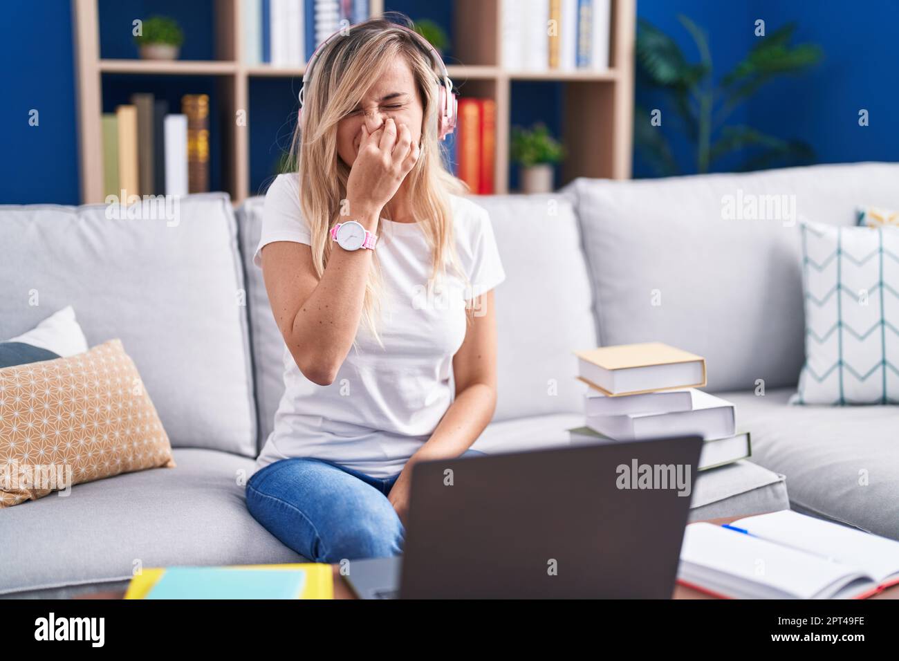 Young blonde woman studying using computer laptop at home smelling ...
