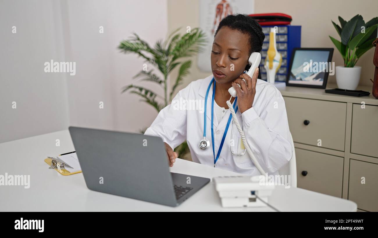 African american woman doctor using laptop talking on telephone at ...