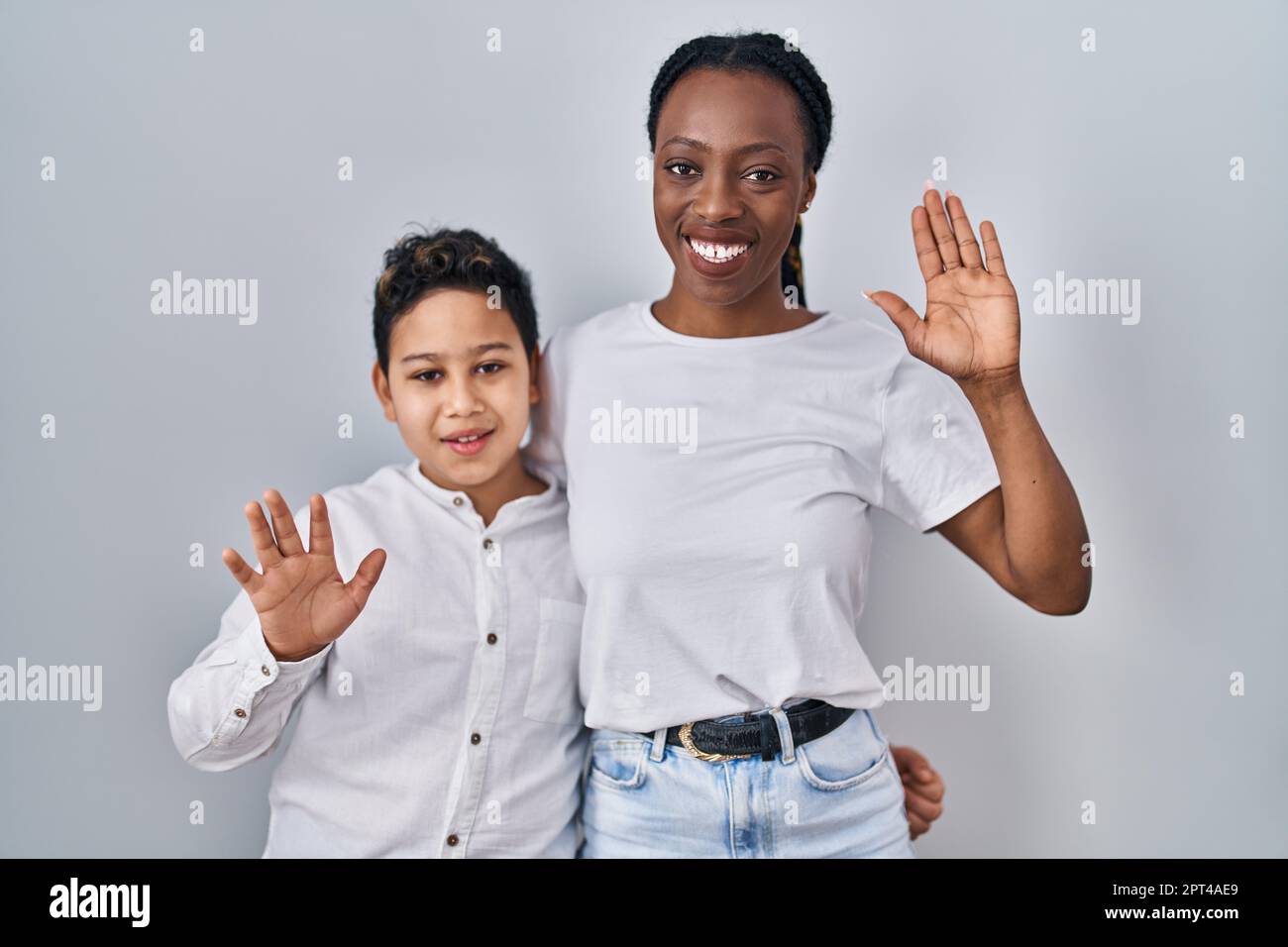Young mother and son standing together over white background waiving ...