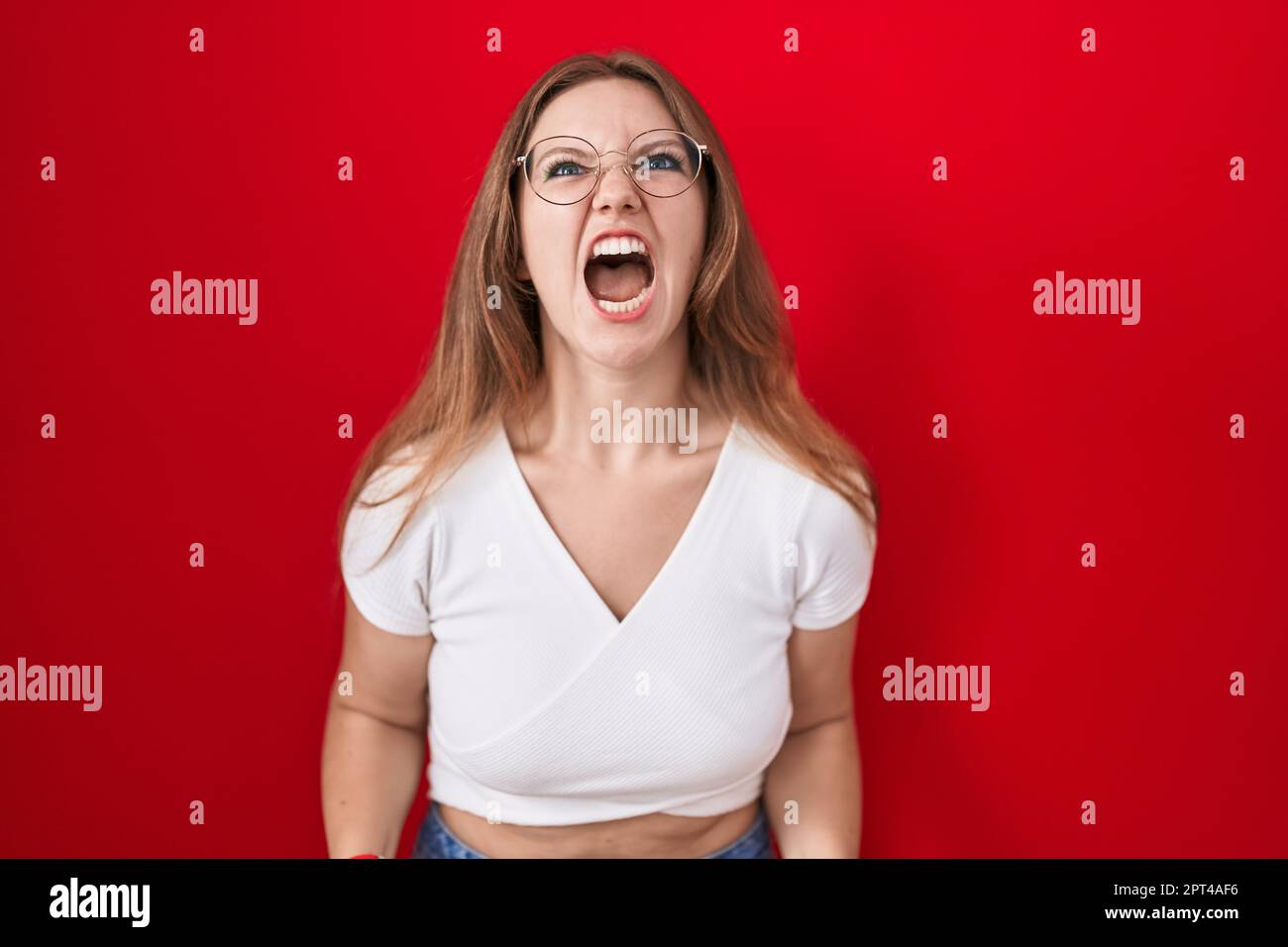 Young caucasian woman standing over red background angry and mad ...