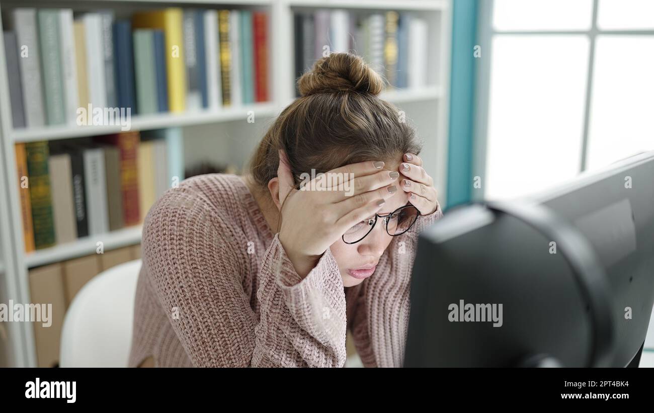 Young beautiful hispanic woman student using computer stressed at ...