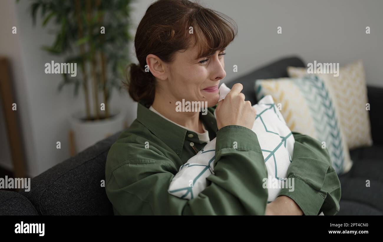 Young caucasian woman crying sitting on the sofa hugging pillow at home ...