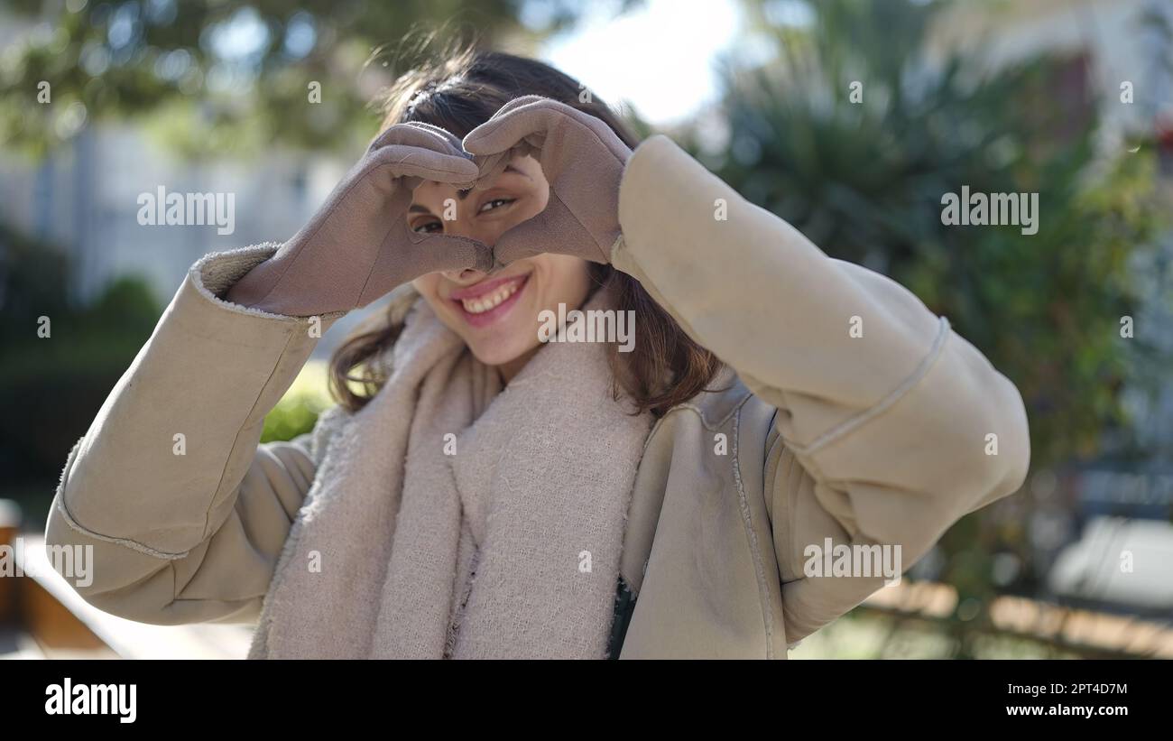 Young caucasian woman doing heart shape with hands over eye at park ...