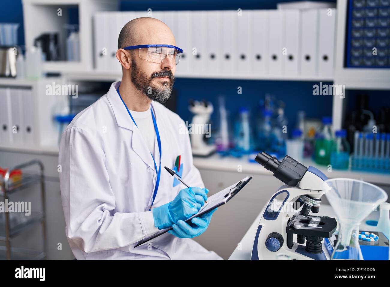 Young bald man scientist writing report working at laboratory Stock ...