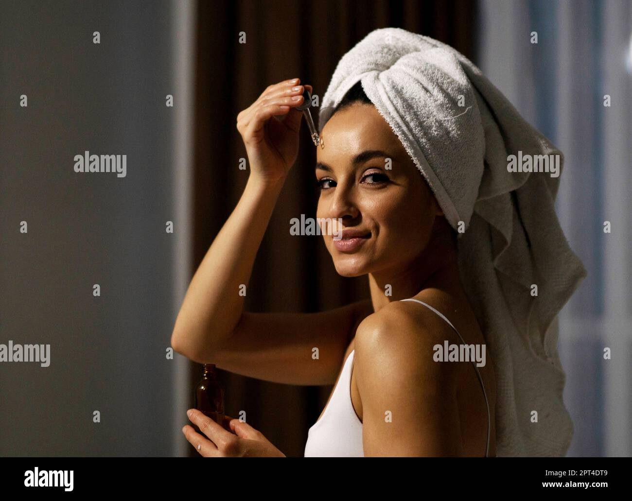 Caucasian pretty young joyful female using facial serum at home ...