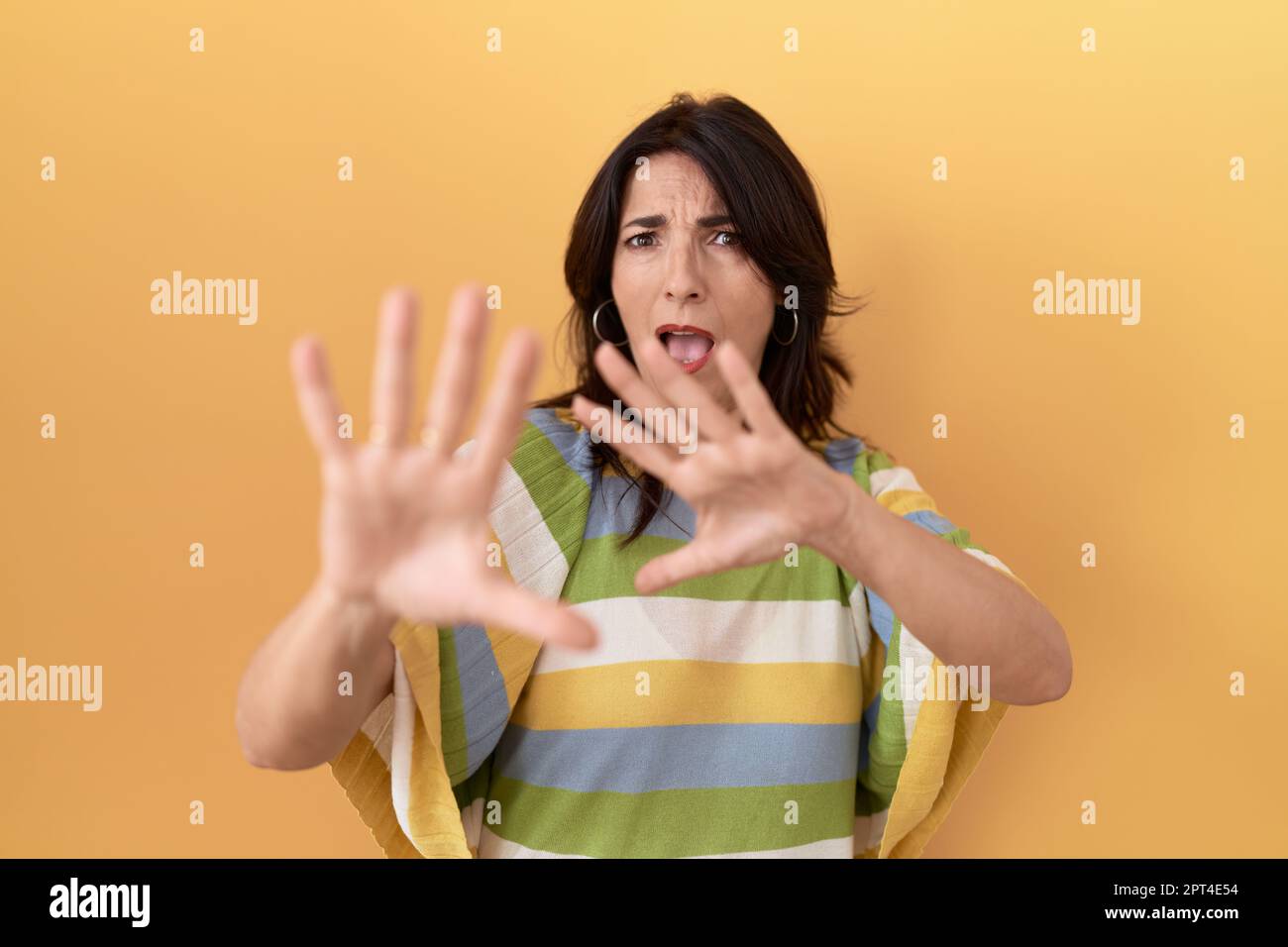 Middle age hispanic woman standing over yellow background afraid and ...