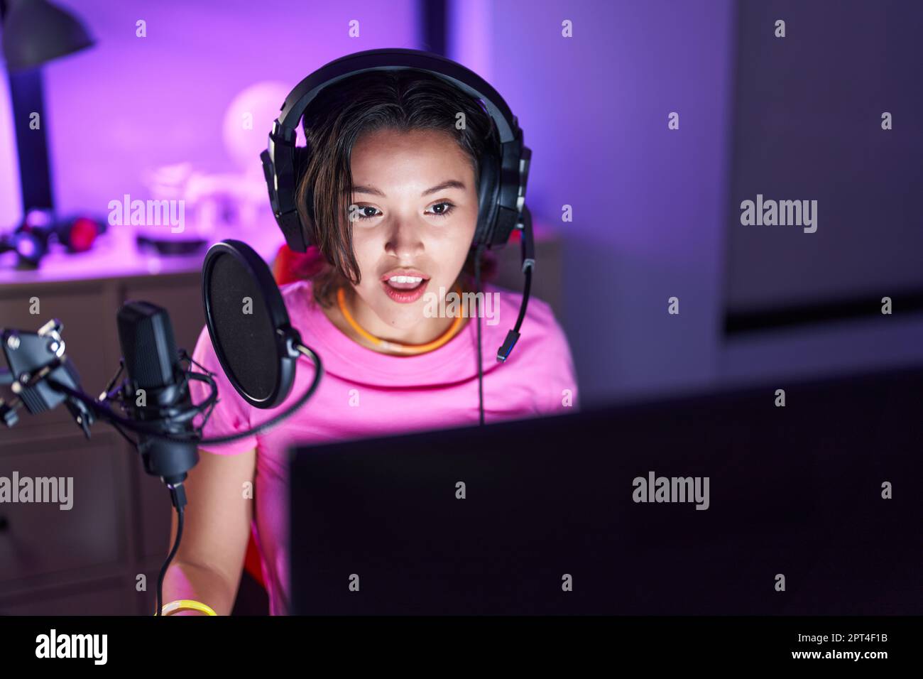 Hispanic young woman playing video games scared and amazed with open ...