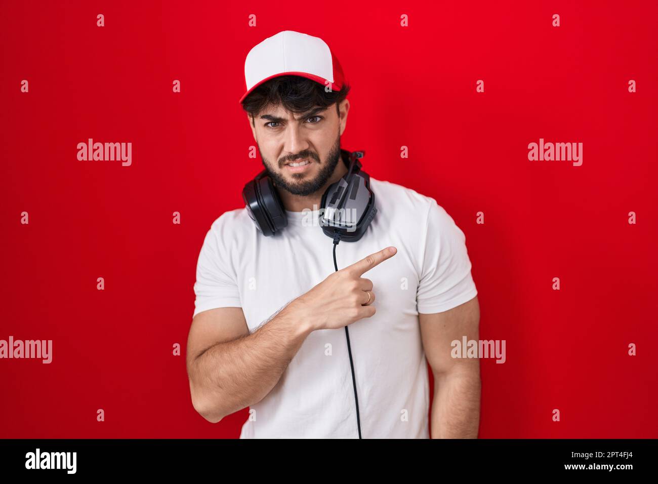 Hispanic man with beard wearing gamer hat and headphones pointing aside ...