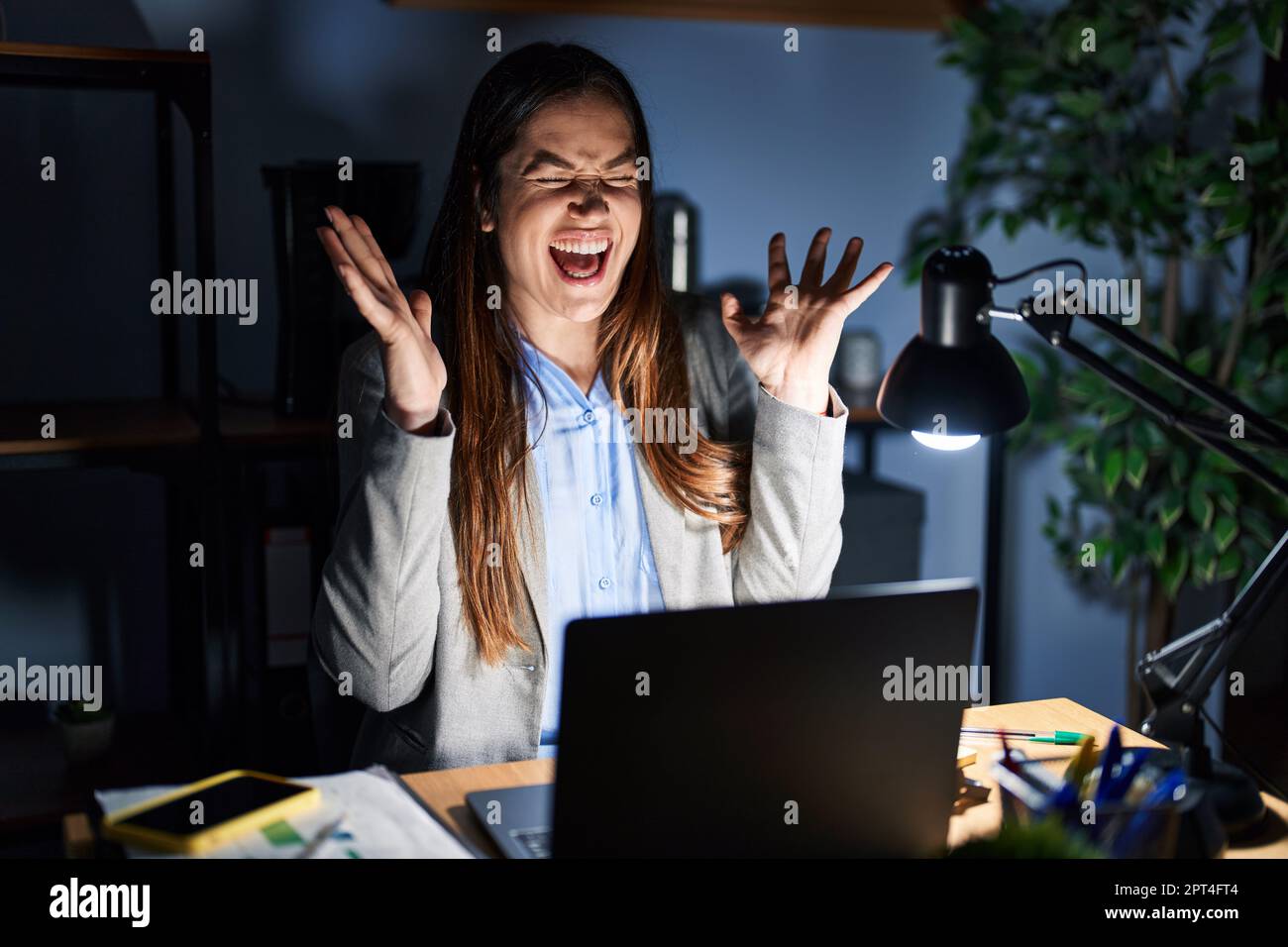 Young brunette woman working at the office at night celebrating mad and ...