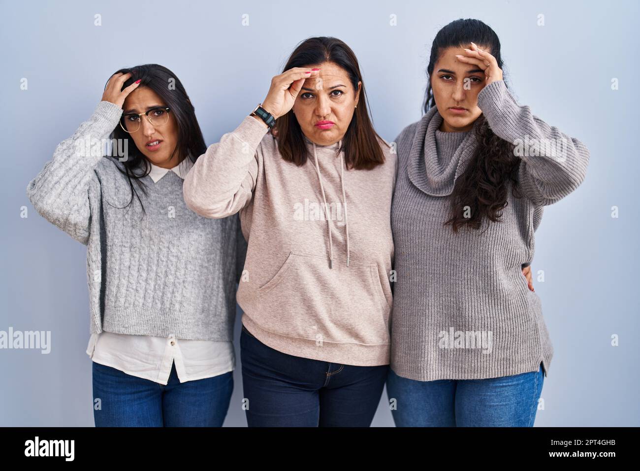 Mother and two daughters standing over blue background worried and ...