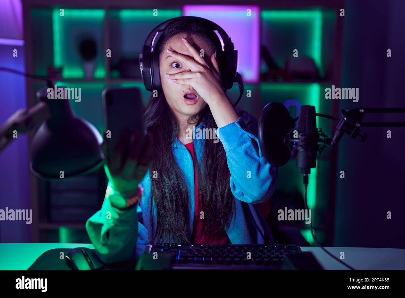 Young asian woman playing video games with smartphone peeking in shock ...