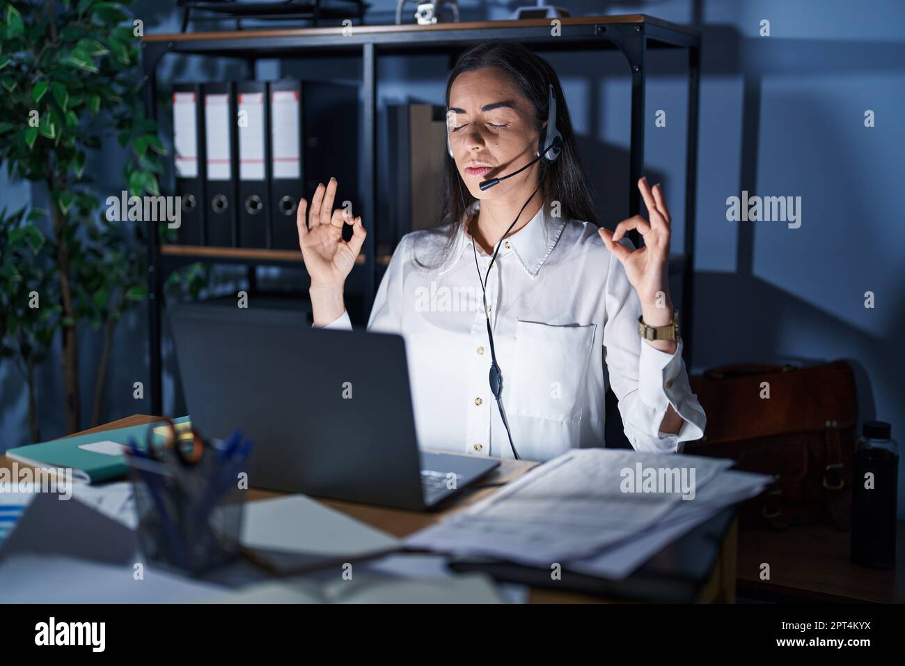 Young brunette woman wearing call center agent headset working late at ...