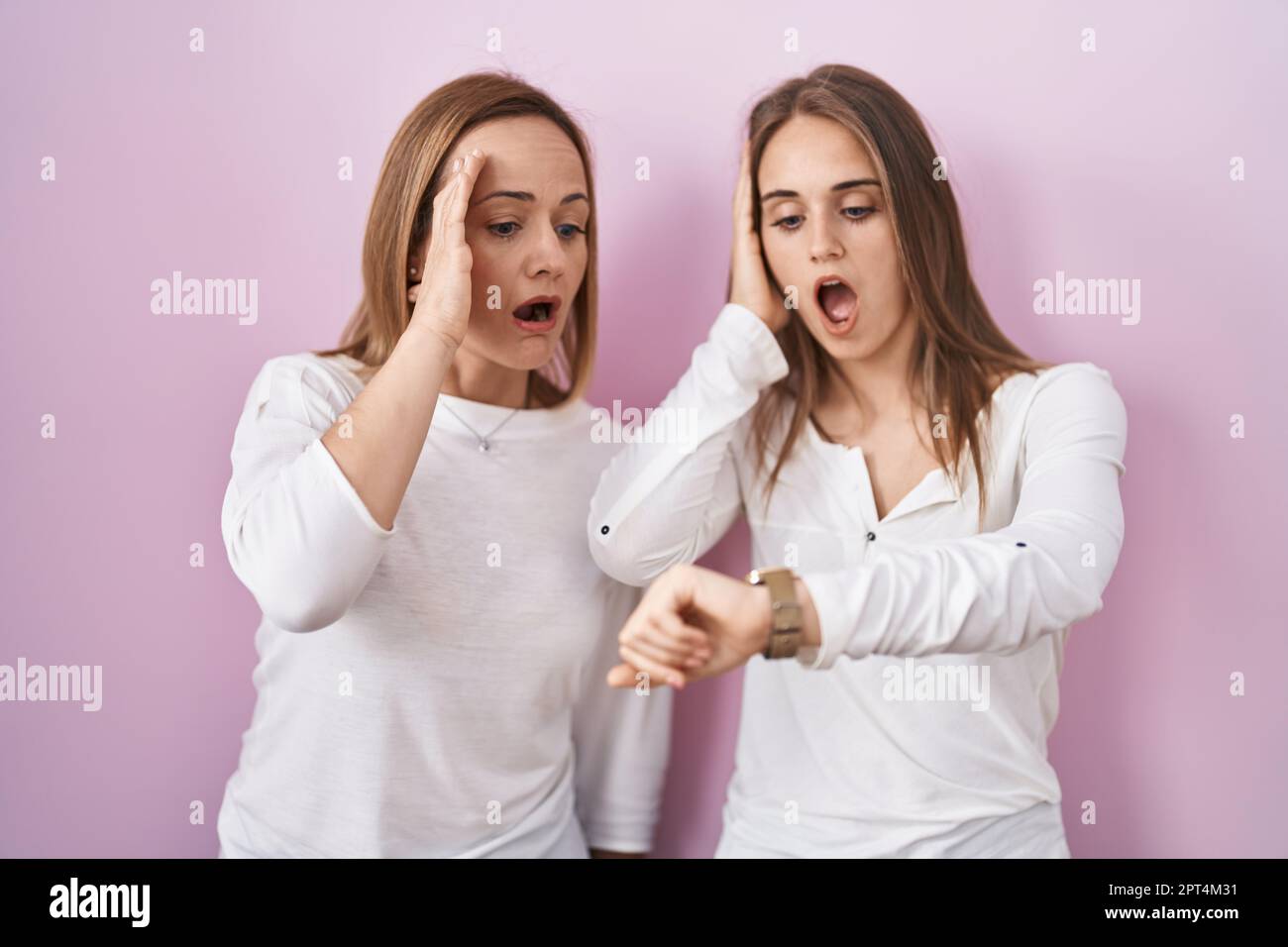 Middle age mother and young daughter standing over pink background ...