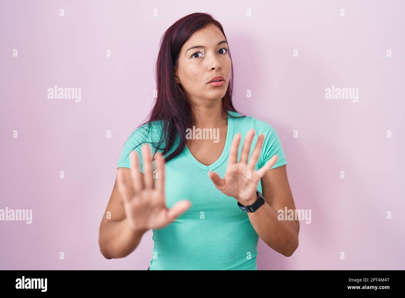 Young hispanic woman standing over pink background moving away hands ...