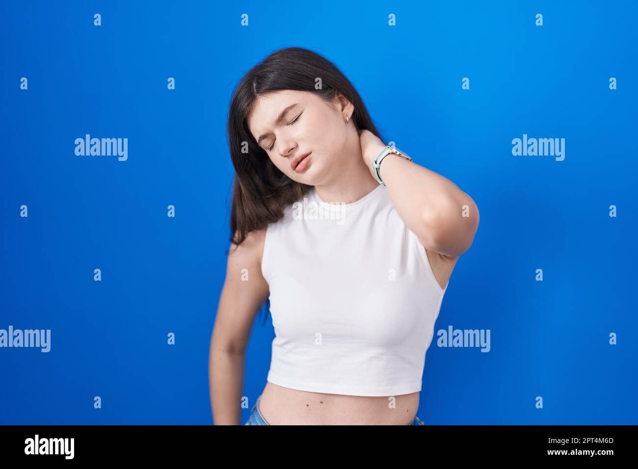Young caucasian woman standing over blue background suffering of neck ...