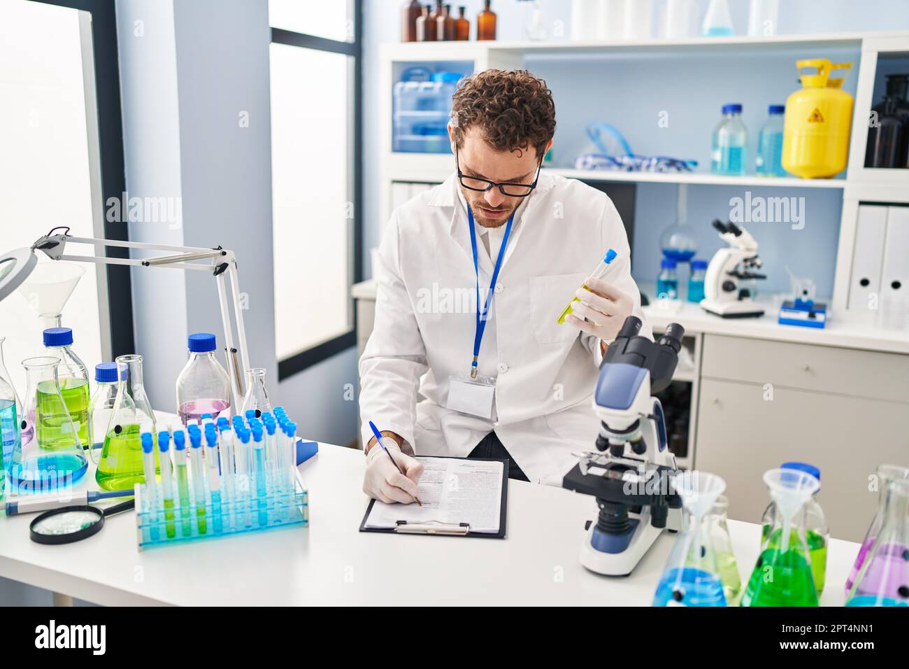 Young hispanic man scientist holding test tube write on document at ...