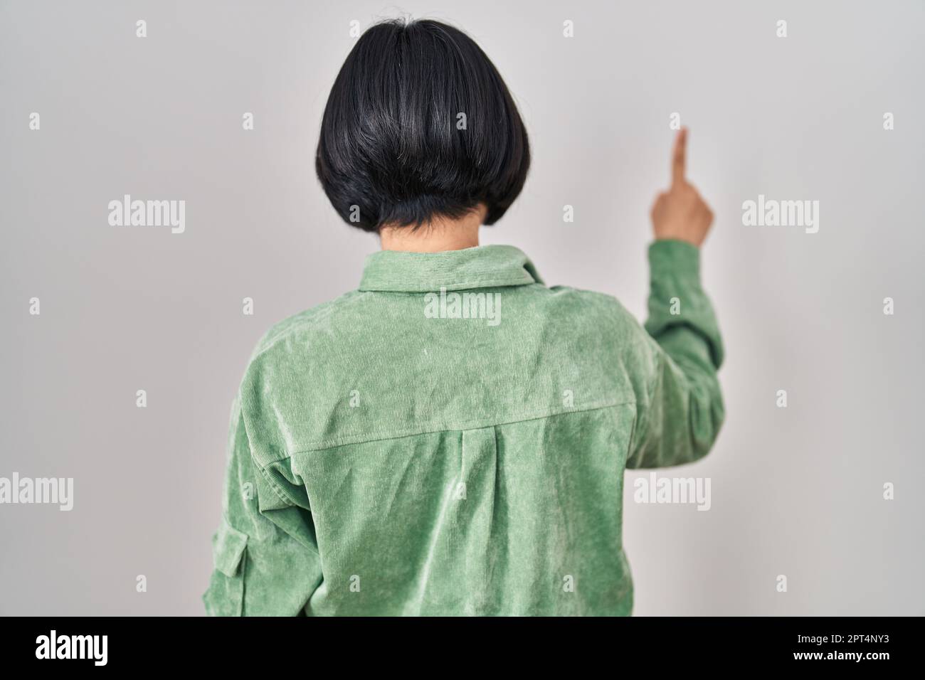 Young asian woman standing over white background posing backwards ...