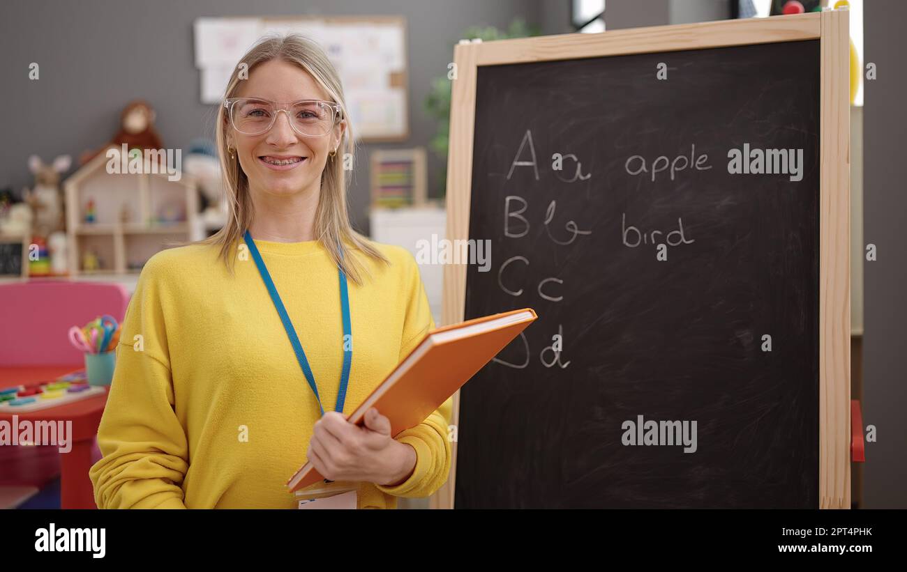 Young blonde woman preschool teacher writing vocabulary exercise on ...