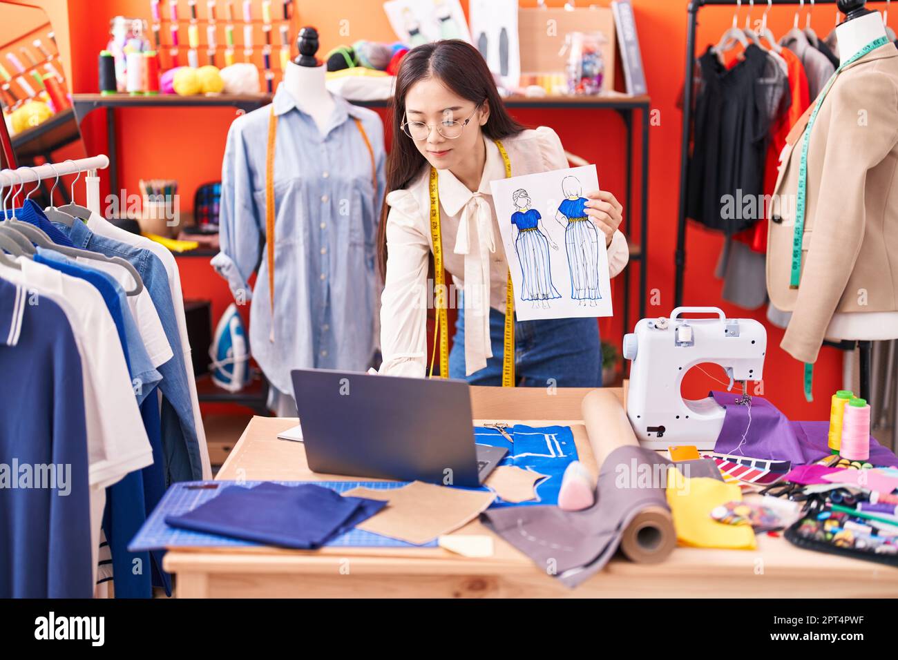 Young chinese woman tailor having video call showing clothing design at ...