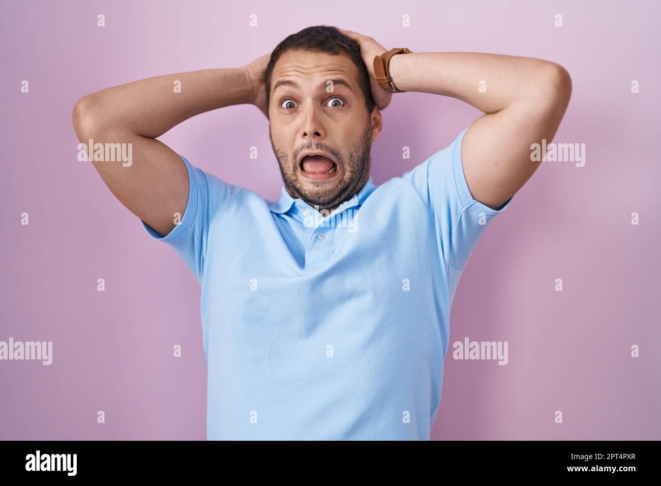 Hispanic man standing over pink background crazy and scared with hands ...