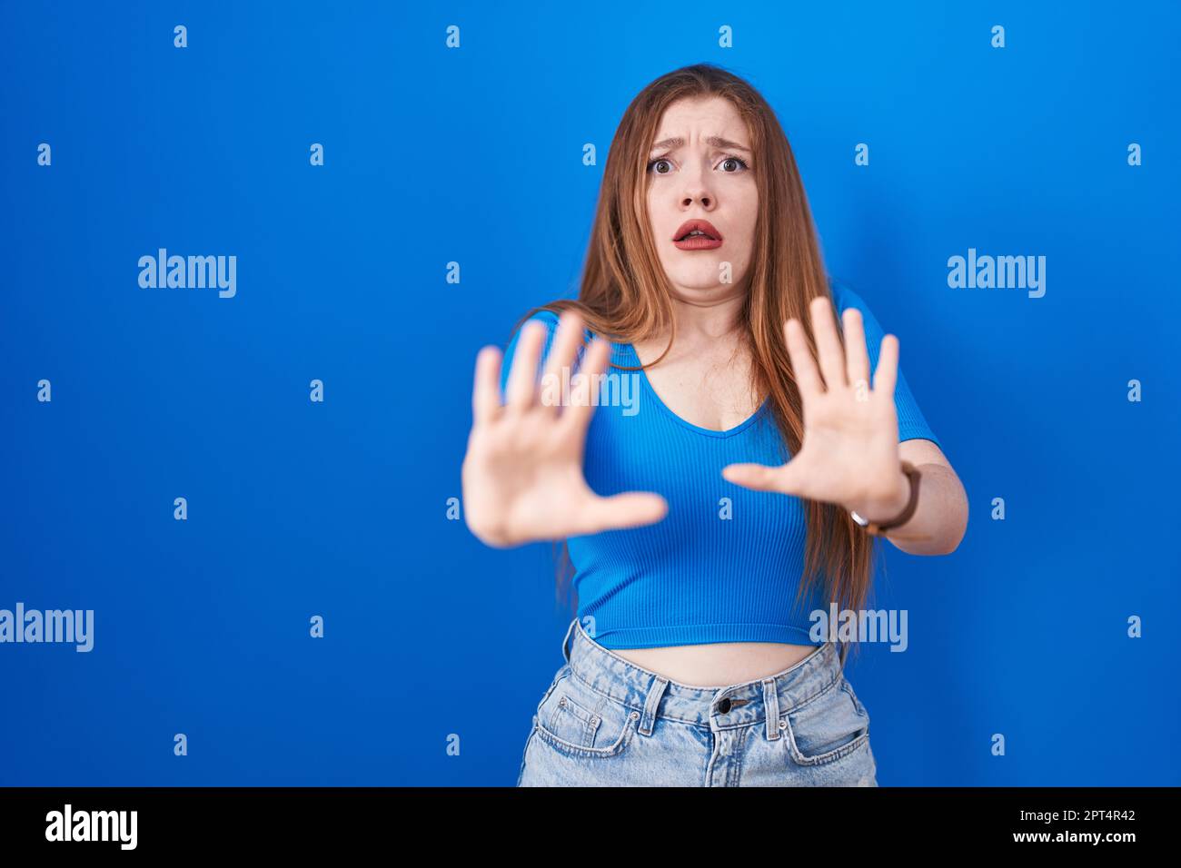 Redhead woman standing over blue background afraid and terrified with ...