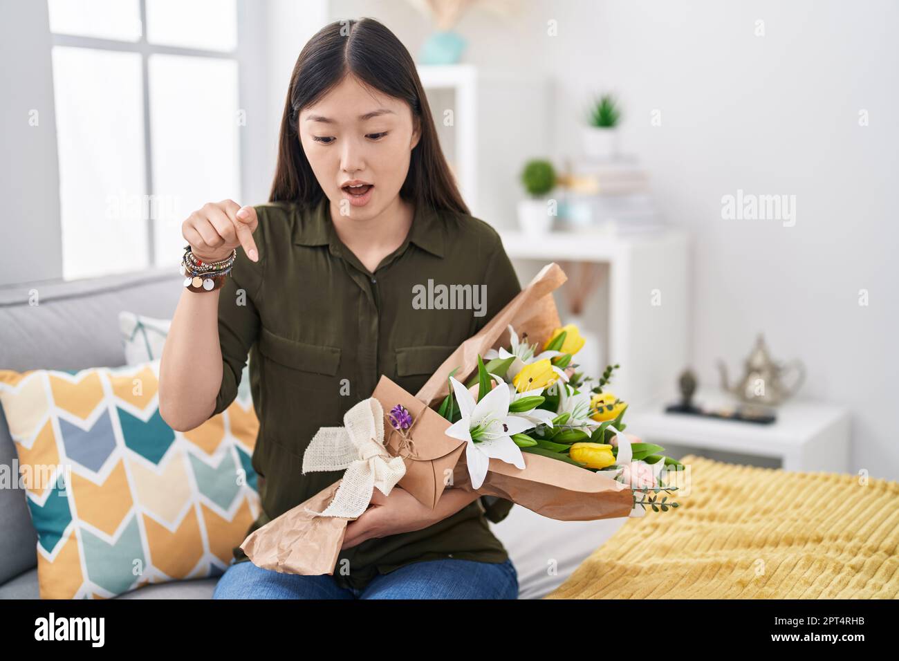 Chinese young woman holding bouquet of white flowers pointing down with ...