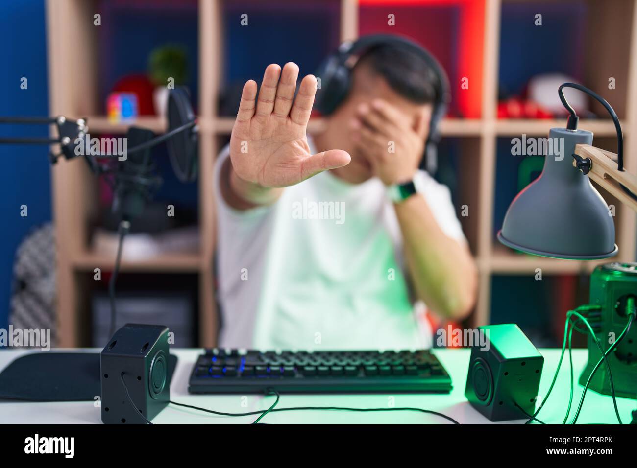Young hispanic man playing video games covering eyes with hands and ...
