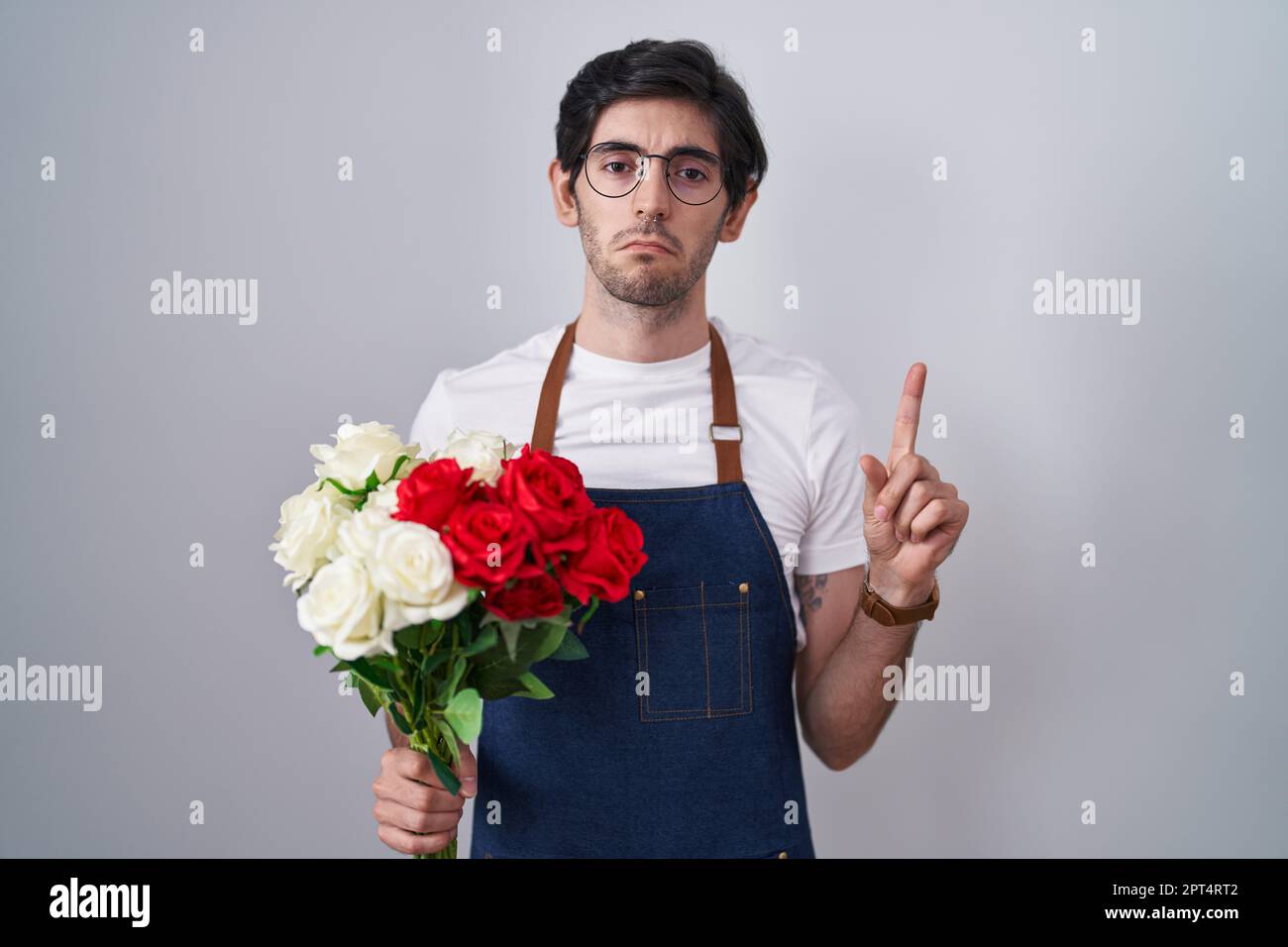 Young hispanic man holding bouquet of white and red roses pointing up ...
