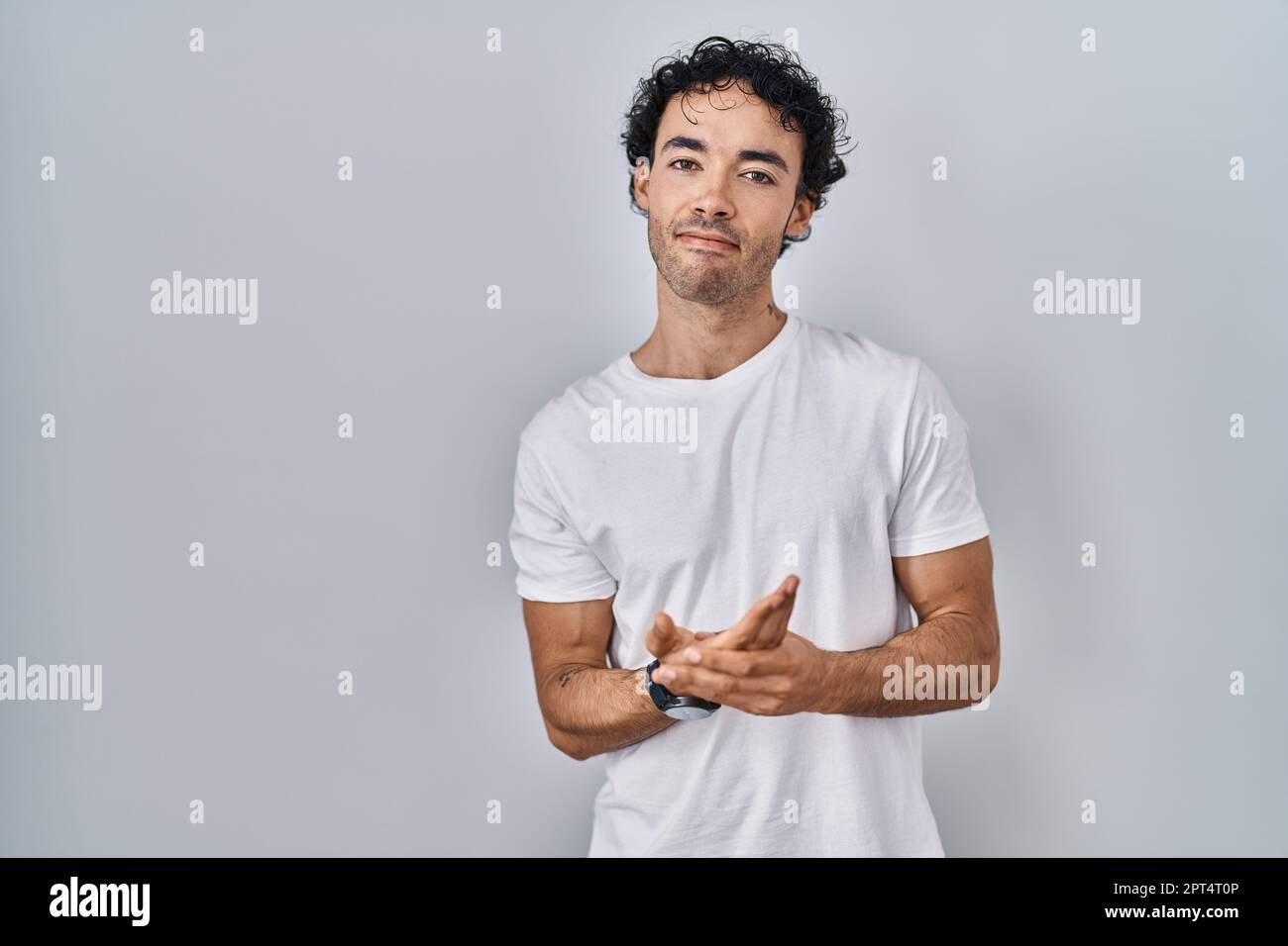 Hispanic man standing over isolated background with hands together and ...