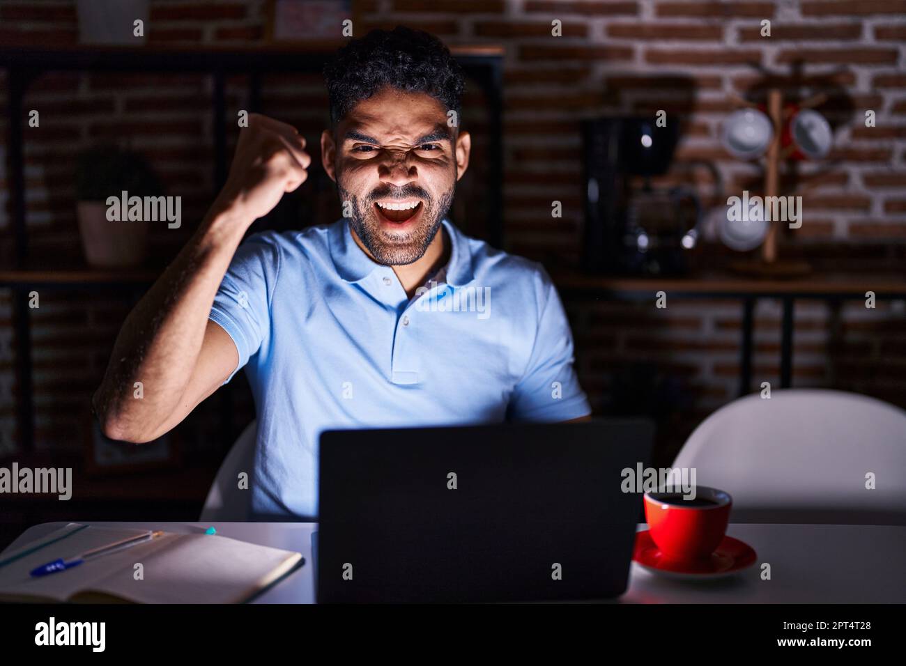 Hispanic man with beard using laptop at night angry and mad raising ...