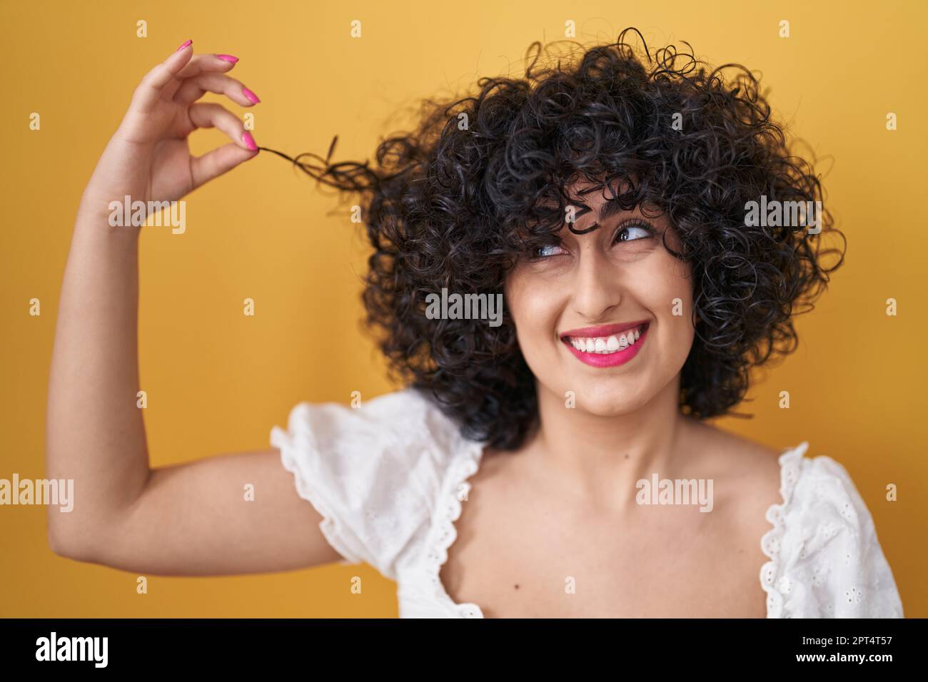 Young brunette woman with curly hair holding curl smiling looking to ...